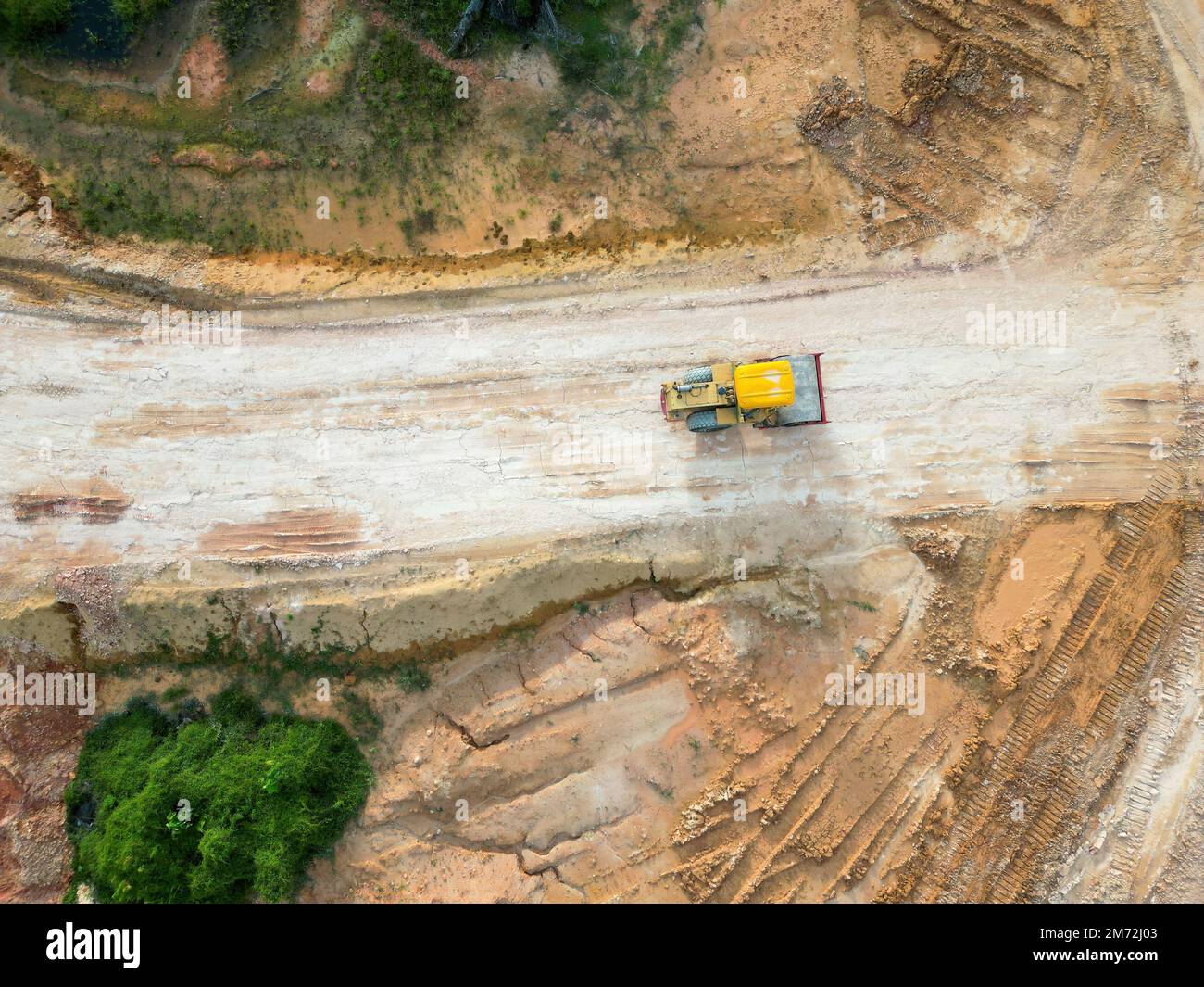 An aerial top view of a bulldozer cultivating a field of an oil palm ...