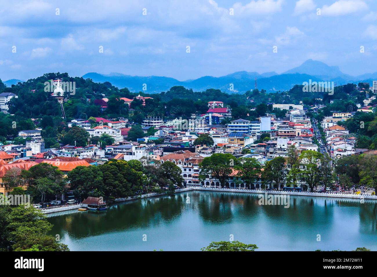An aerial view of Kandy Lake surrounded by green mountains and building ...
