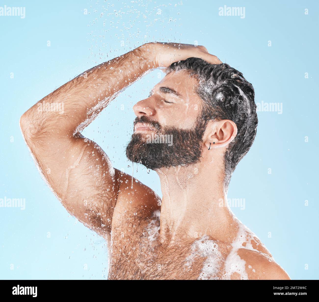 Face, water splash and shampoo shower of man in studio isolated on a blue background. Water ...