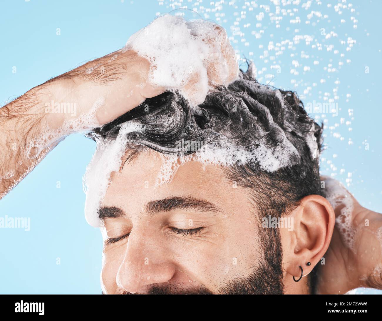 Face, water splash and man in shower with shampoo in studio on a blue ...