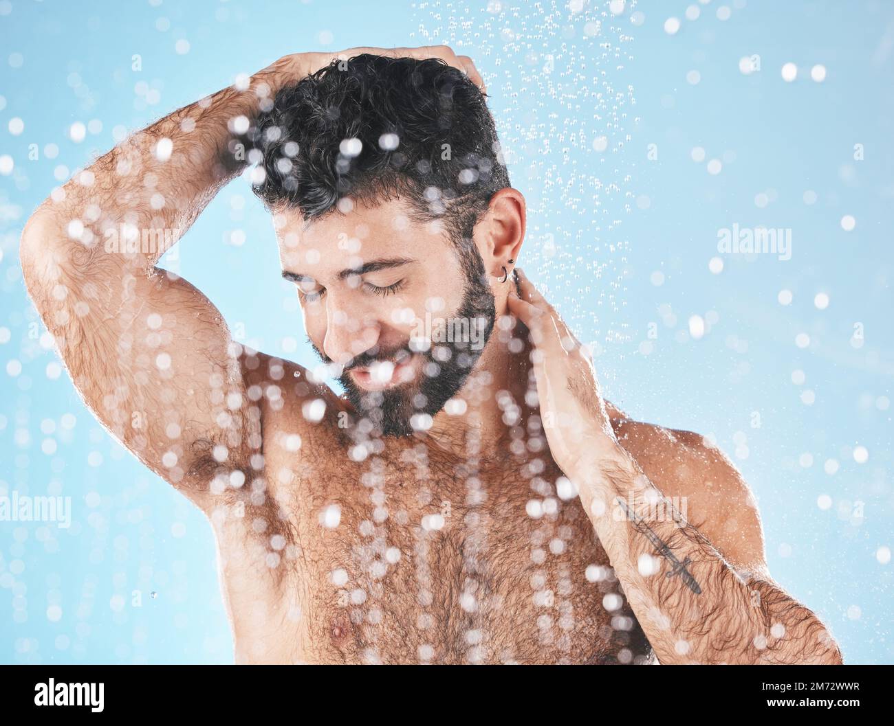 Water splash, face and man in shower for skincare in studio isolated on a blue background. Water ...
