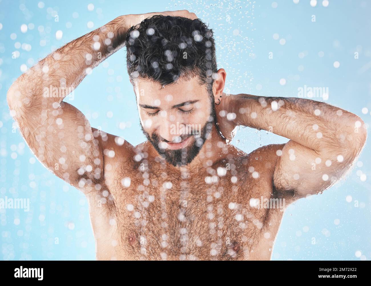 Face, water splash and skincare shower of man in studio isolated on a blue background ...