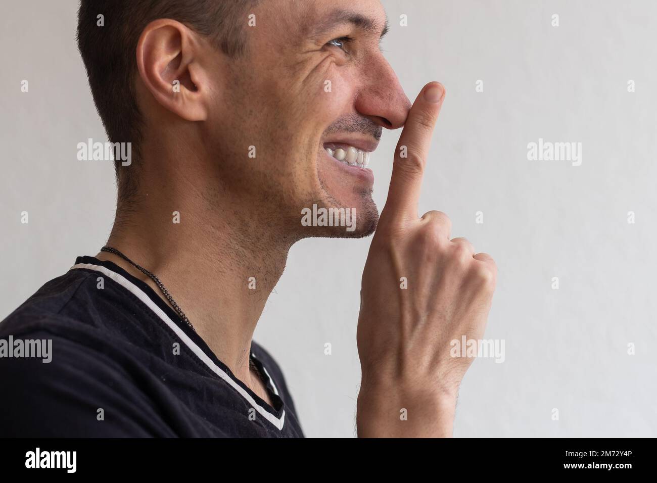 Positive smiling man with beard holding finger near lips showing shh ...
