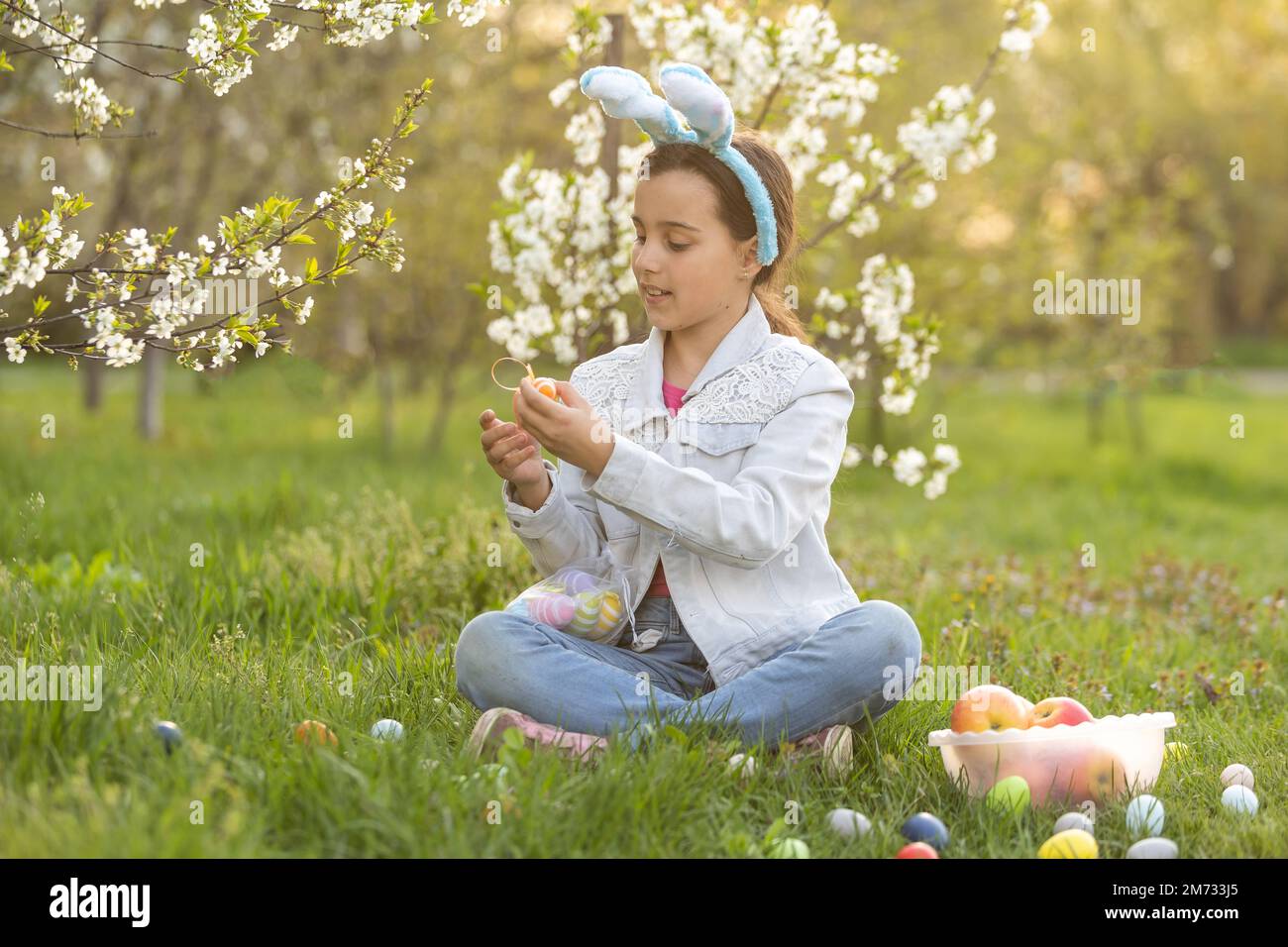 Adorable little girl in bunny ears, blooming tree branch outdoors on a ...