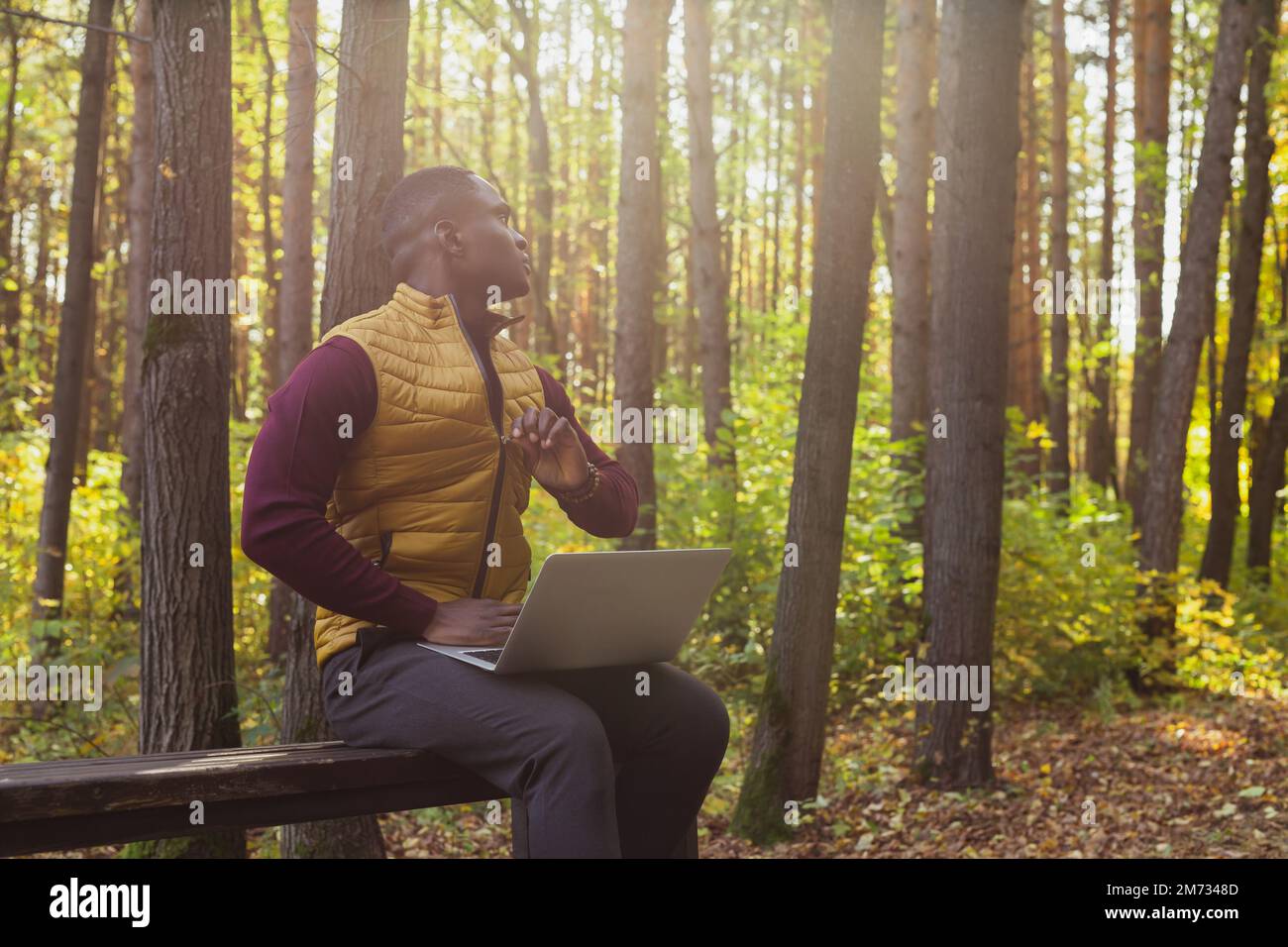 African american man sitting in city park on a bench with laptop ...