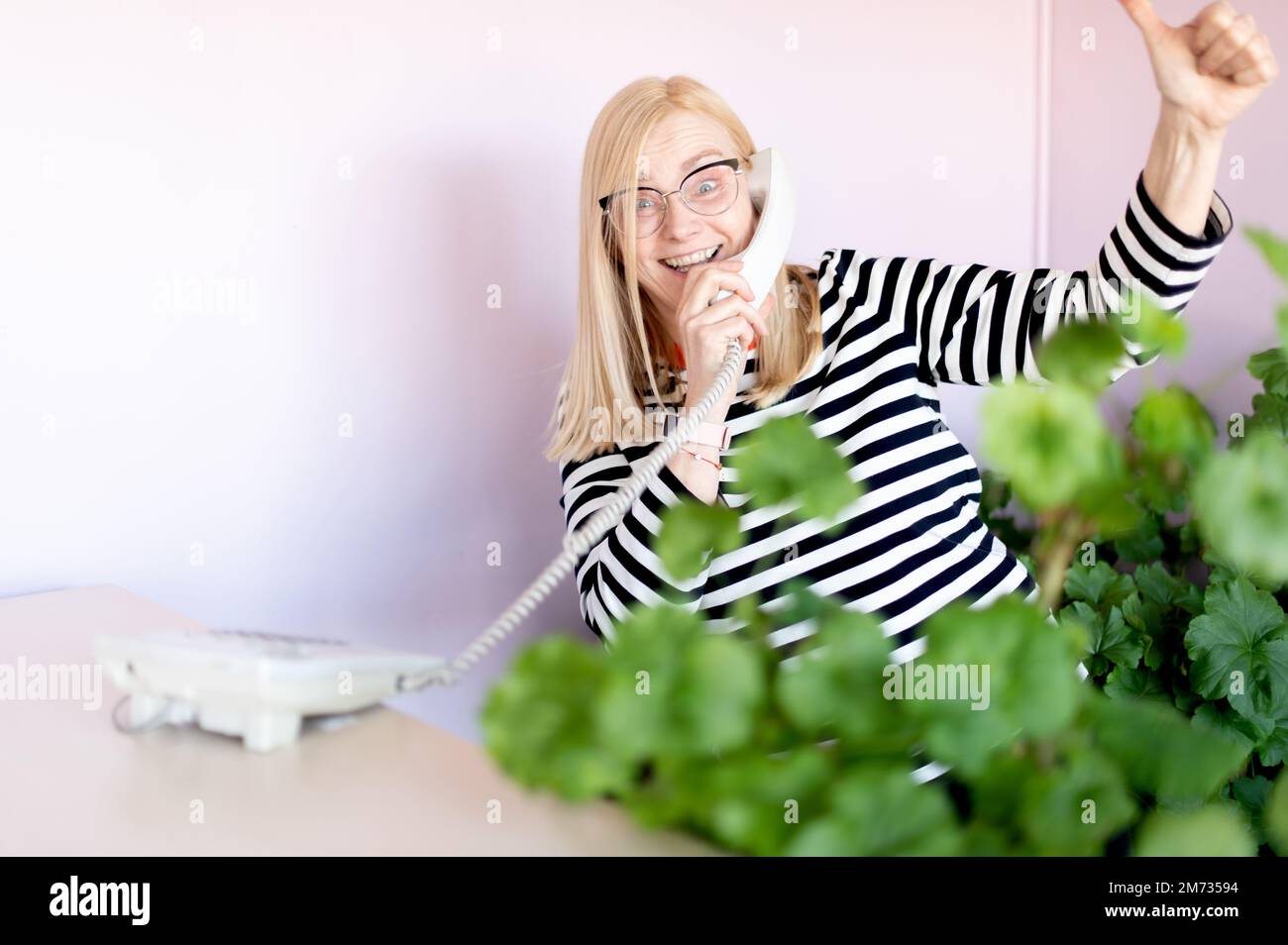 Happy middle-aged woman talking on a landline phone at her workplace ...