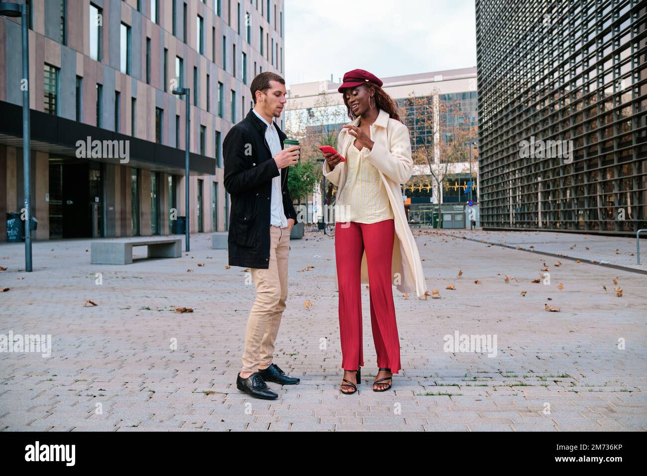 Two business people drinking coffee and using mobile phone outdoors in ...