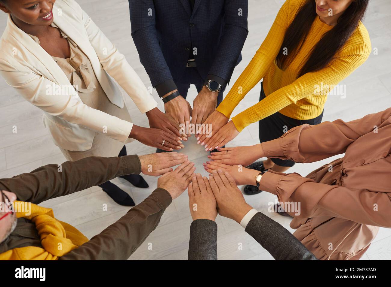 Diverse happy men and women fold their arms together in circle together ...