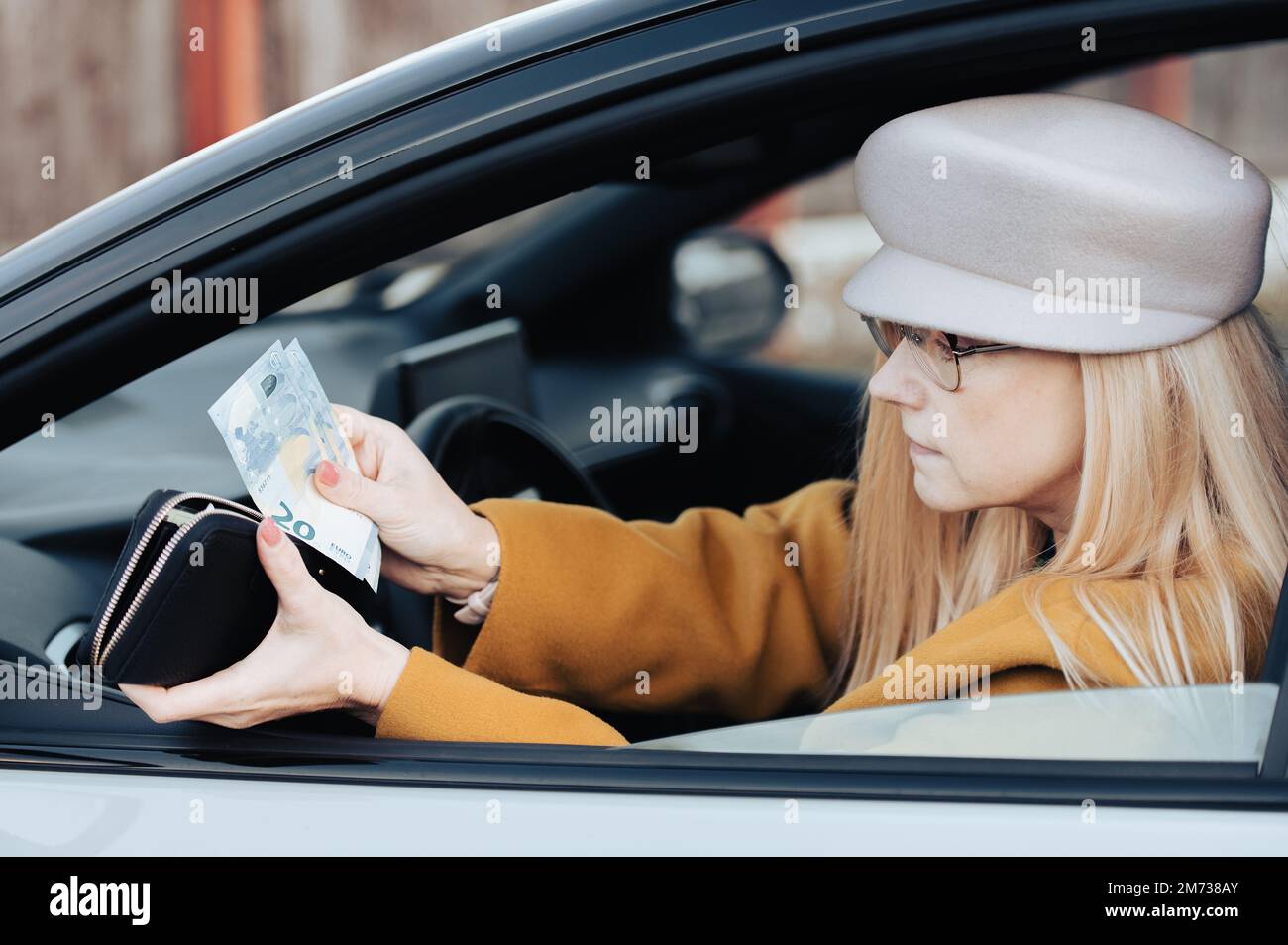 Middle-aged woman sits behind the wheel of car and looks for euro in ...