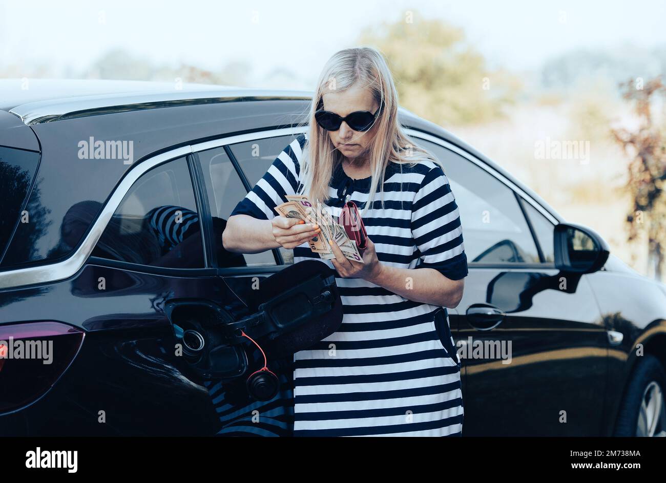 Desperate woman hold cash dollar bills next to car with an open tank ...