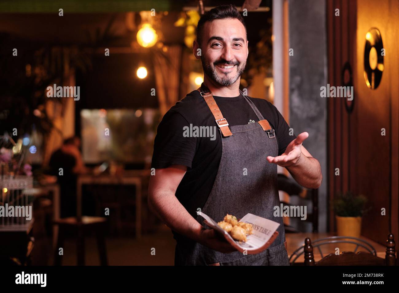 Waiter looking at the camera and smiling while showing plate with food ...