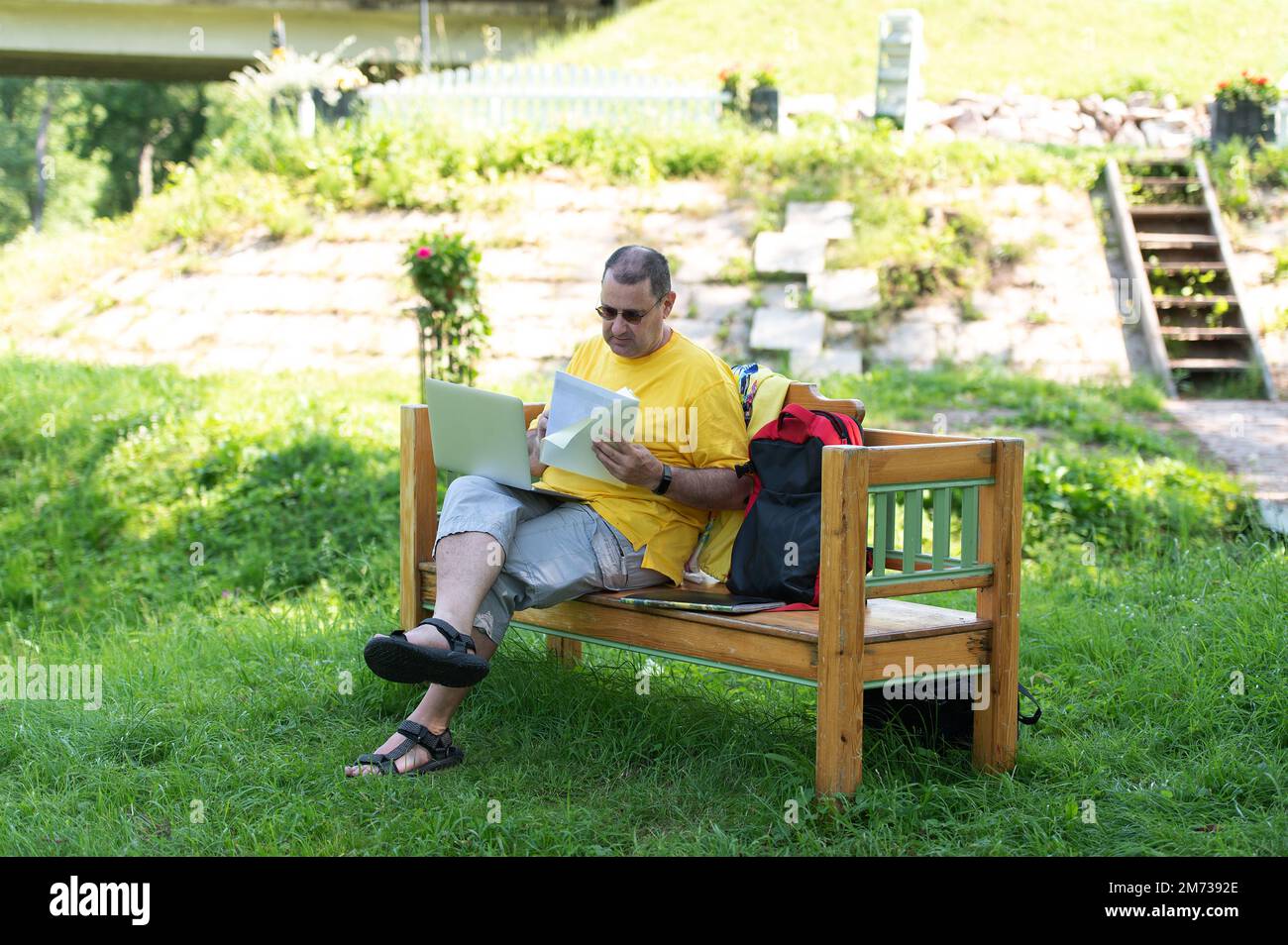 Middle-aged man man sitting on the wooden bench in park and using ...