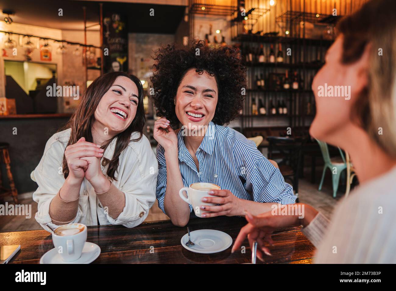 A group of young women talking and laughing sitting on a coffee shop or ...