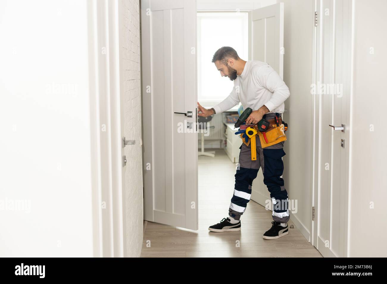 good looking man working as handyman and fixing a door lock in a house ...