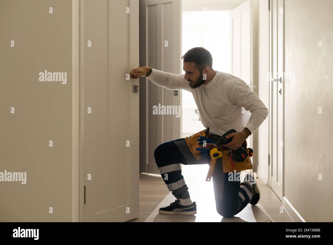 good looking man working as handyman and fixing a door lock in a house ...