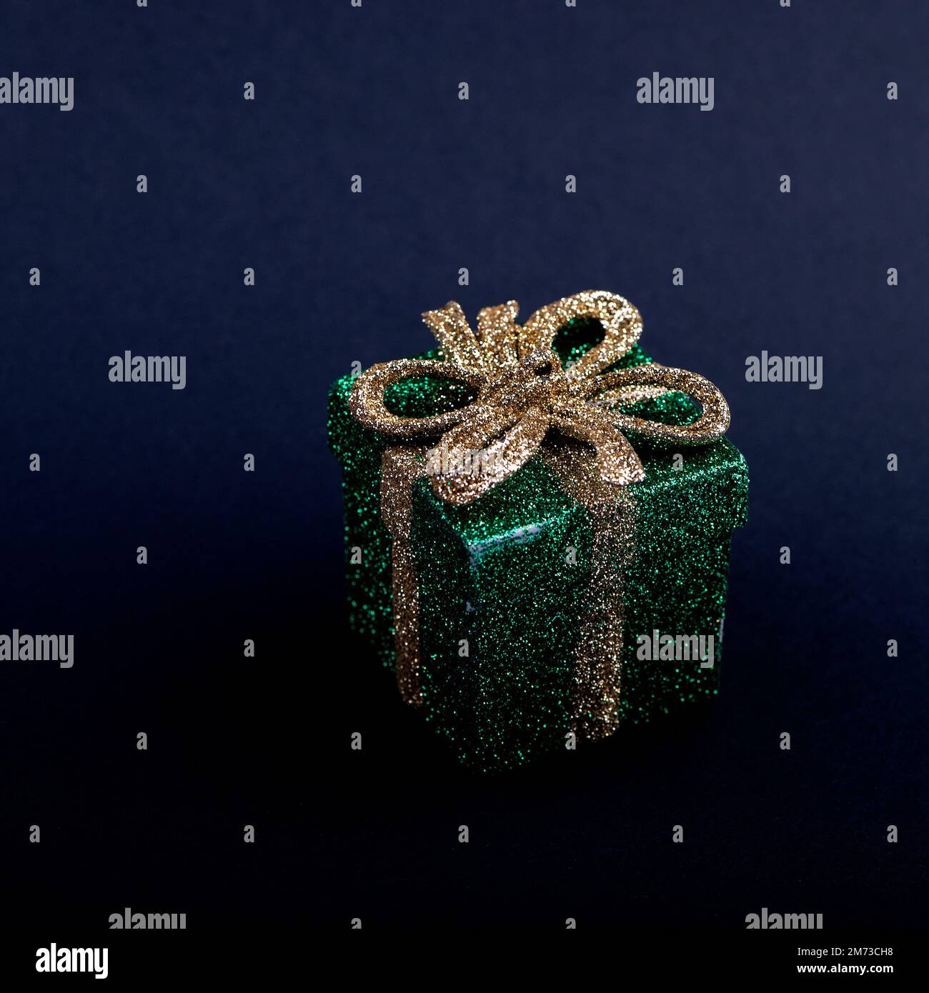 Christmas decor green gift box with shiny gold bow on dark square ...