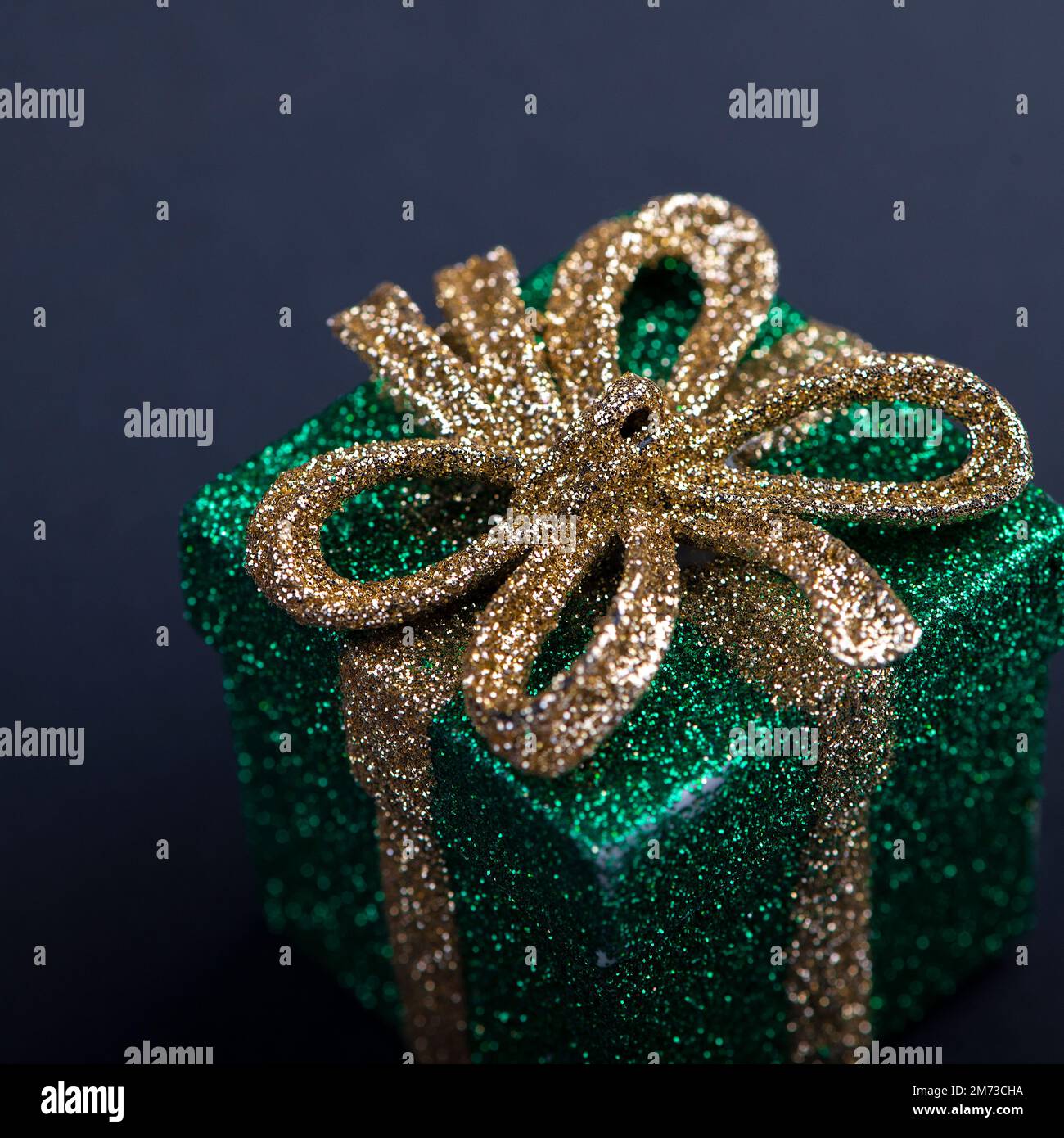 Christmas decor green gift box with shiny gold bow on dark square ...