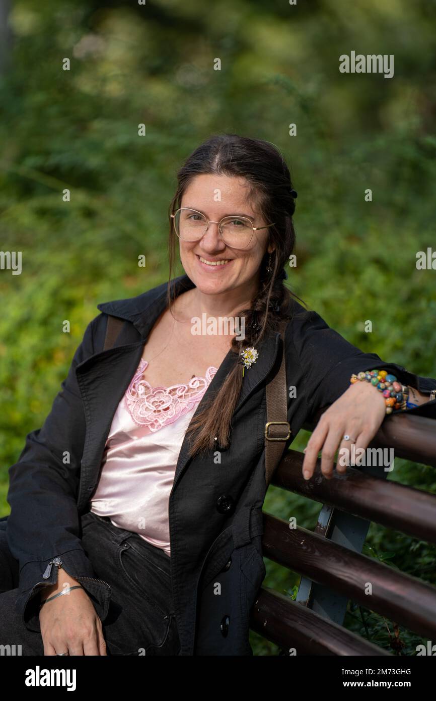 A vertical shot of a white female in specs sitting on a bench and ...