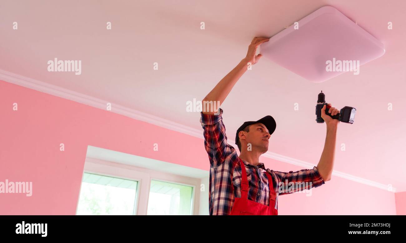 A young man stands on a stepladder and installs a large chandelier on ...