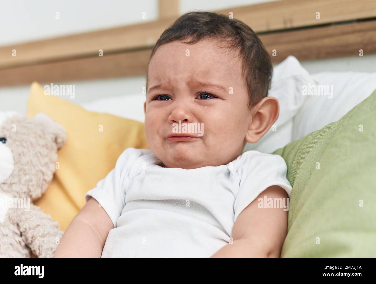 Adorable hispanic baby sitting on bed crying at bedroom Stock Photo - Alamy