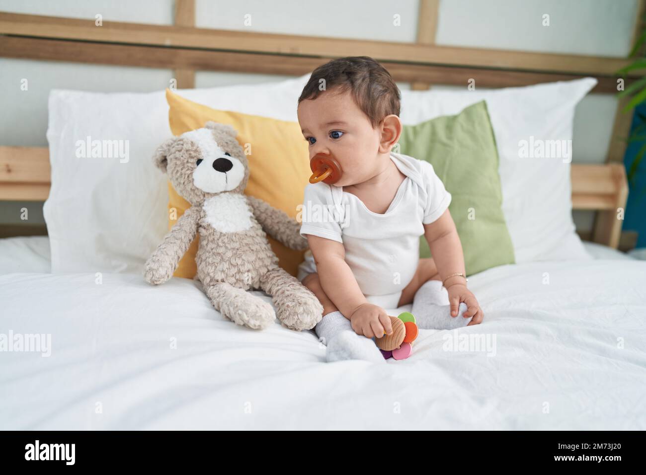 Adorable hispanic baby sucking pacifier sitting on bed at bedroom Stock ...