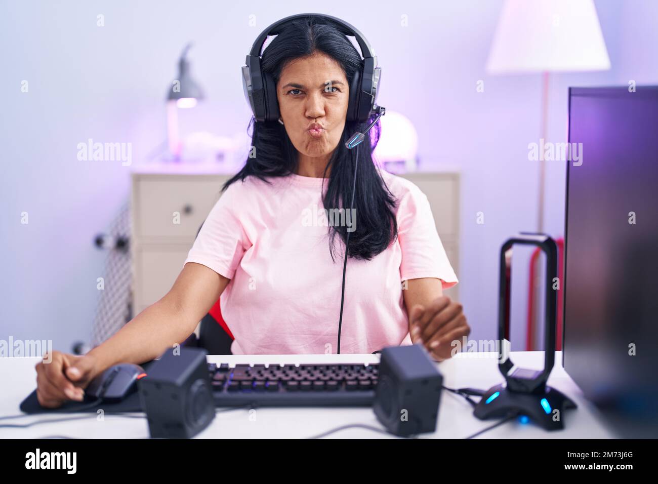 Mature hispanic woman playing video games at home making fish face with ...