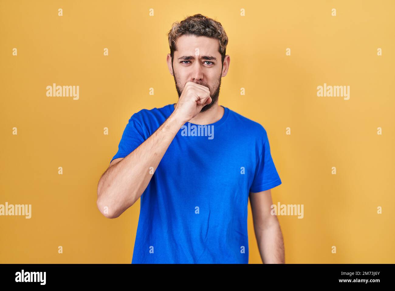 Hispanic man with beard standing over yellow background feeling unwell ...