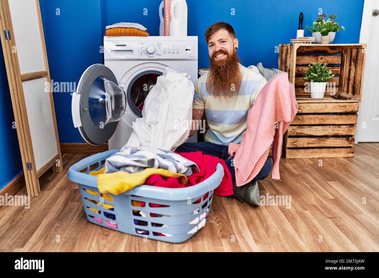 Young redhead man smiling confident washing clothes at laundry room ...