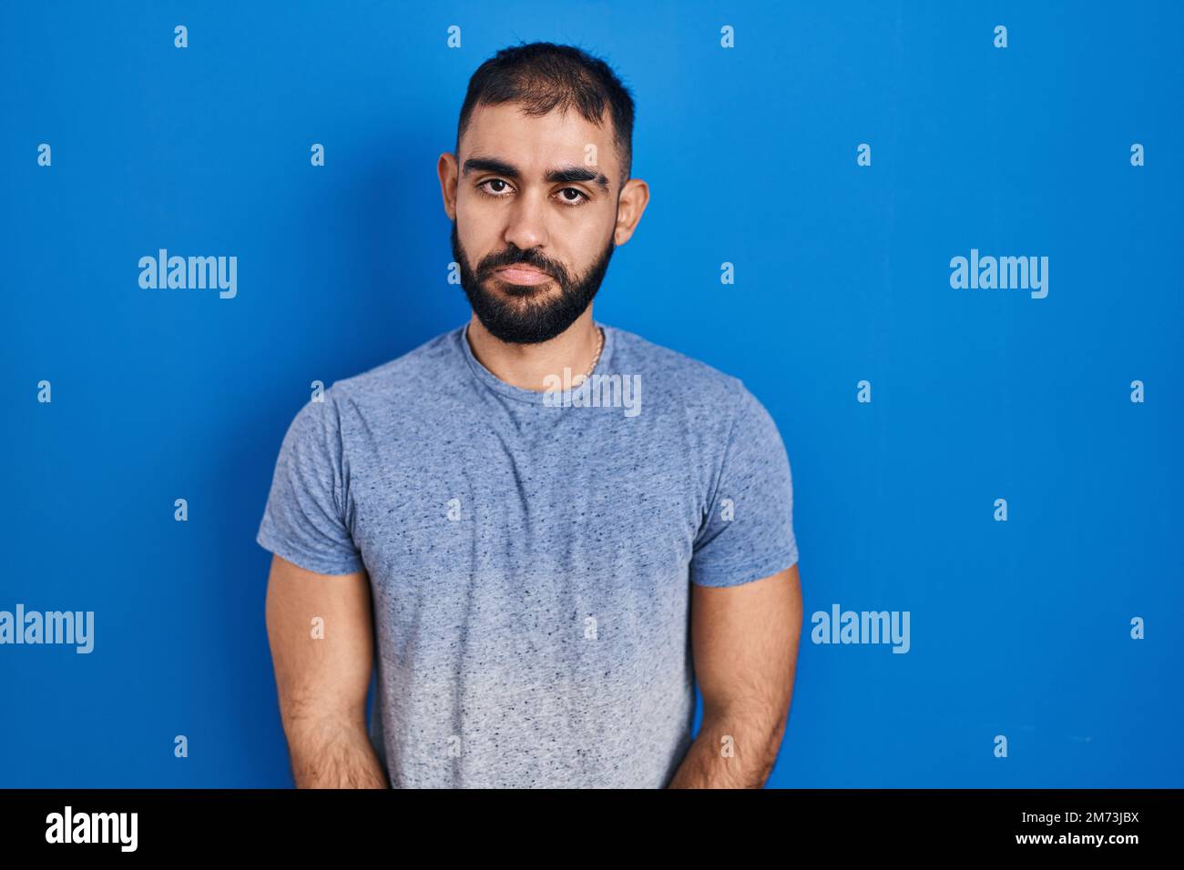 Middle east man with beard standing over blue background depressed and ...