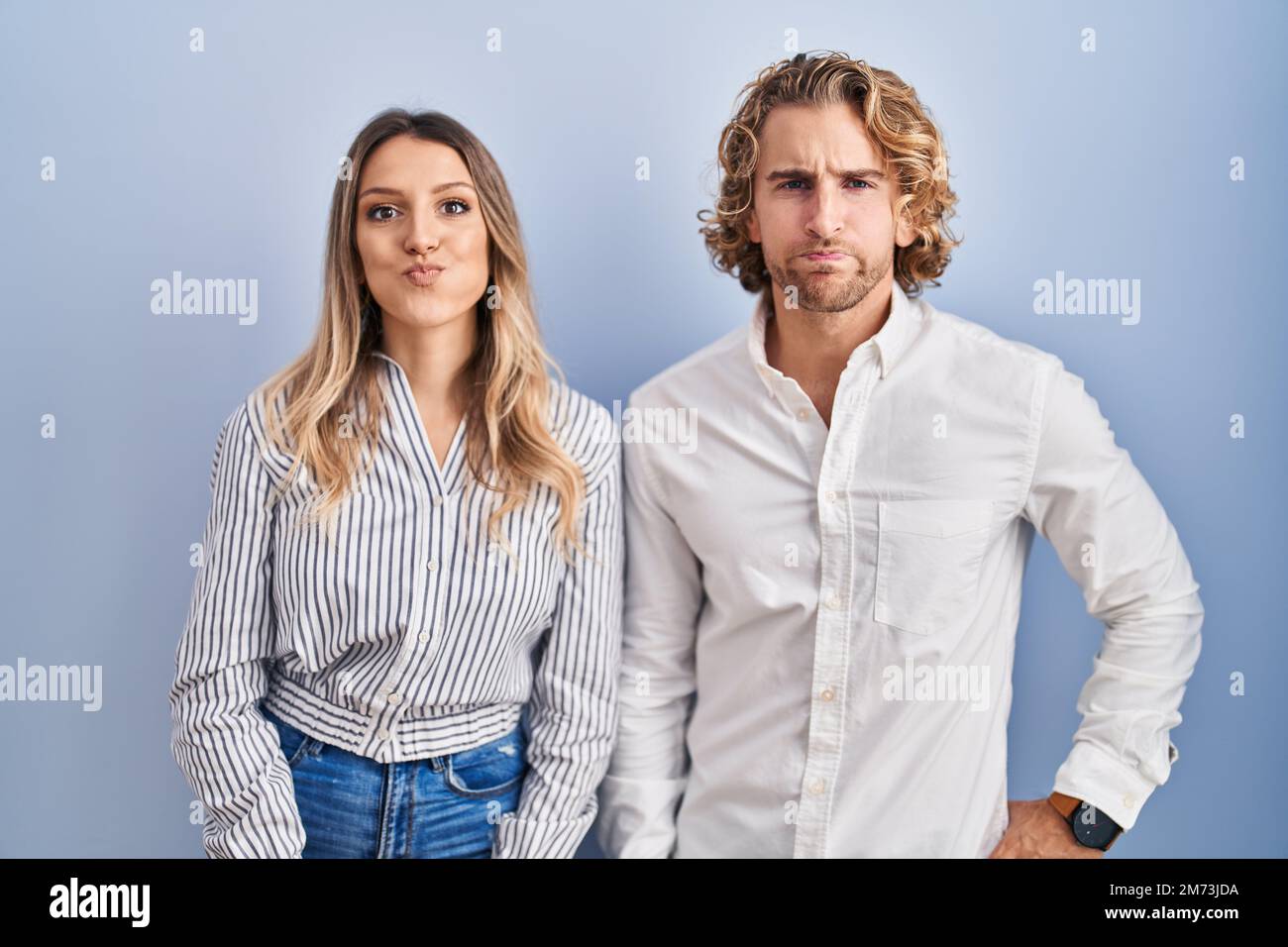 Young couple standing over blue background puffing cheeks with funny ...
