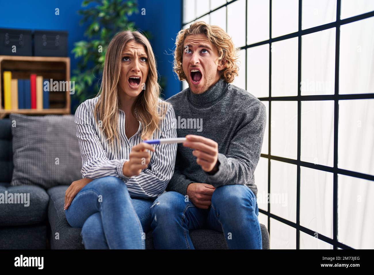 Young couple holding pregnancy test result angry and mad screaming ...