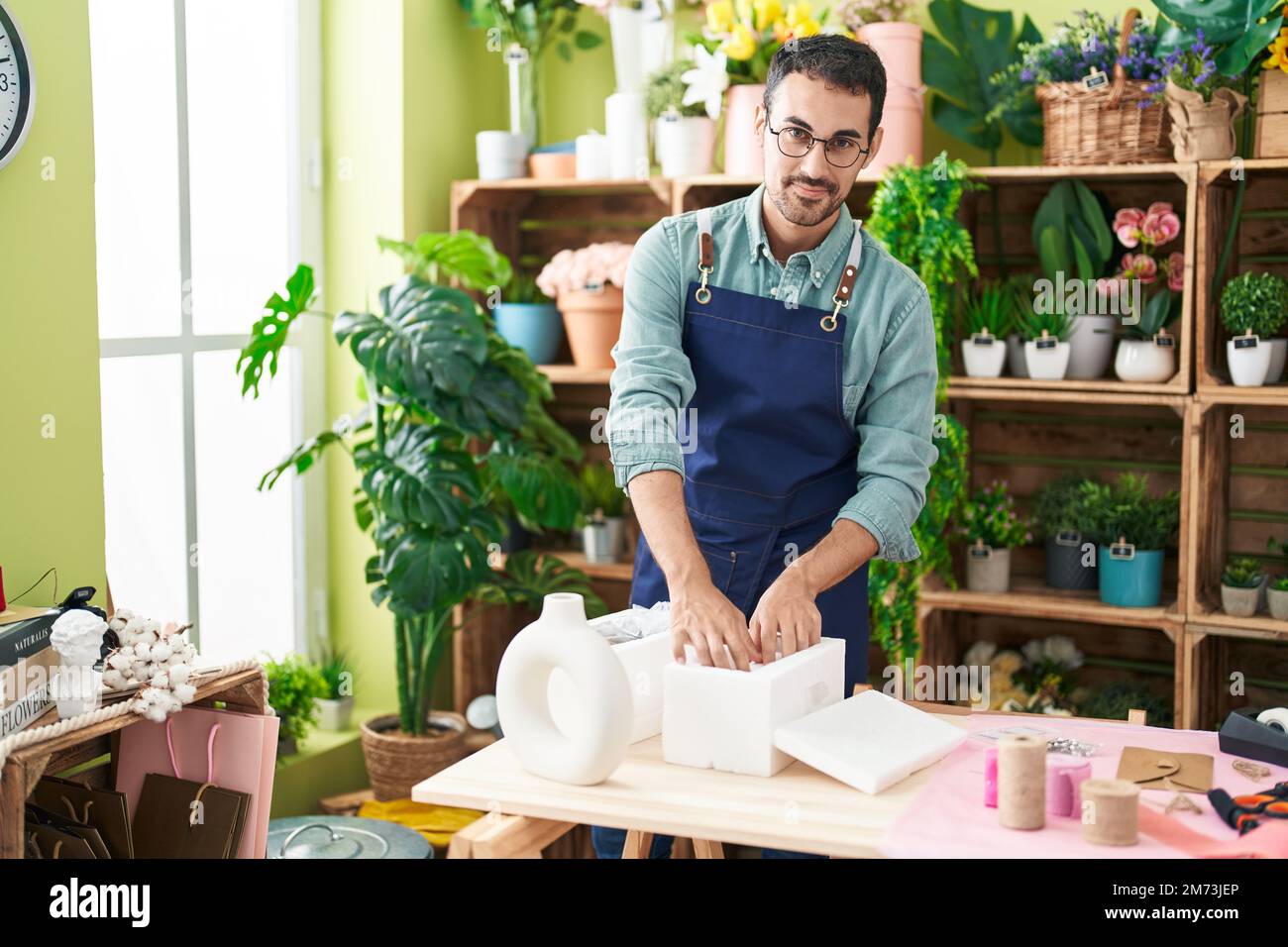 Young hispanic man florist smiling confident unpacking plant pots at ...