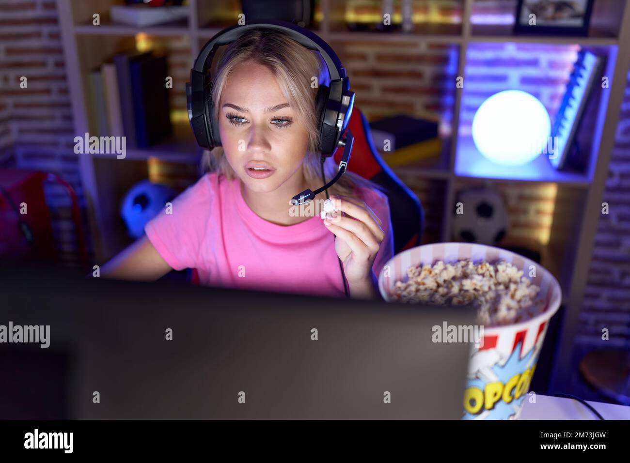 Young blonde woman streamer playing video game eating popcorn at gaming ...