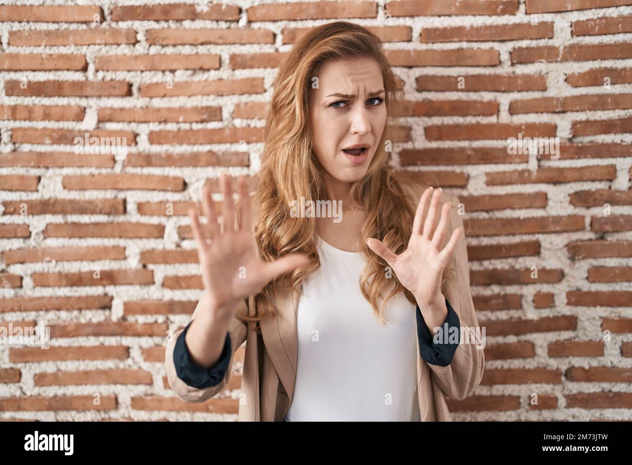 Beautiful blonde woman standing over bricks wall afraid and terrified ...