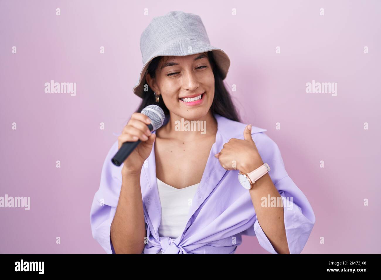 Young hispanic woman singing song using microphone over pink background ...