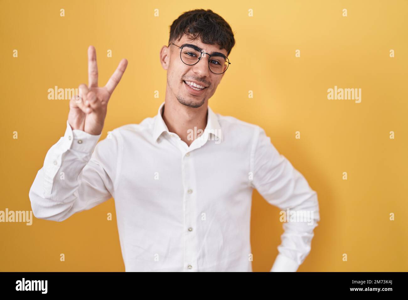 Young hispanic man standing over yellow background smiling looking to ...