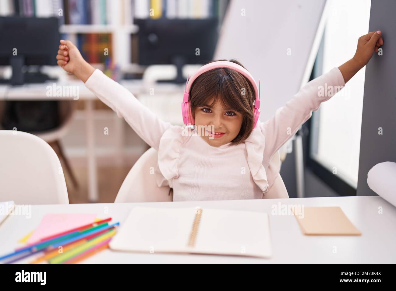 Adorable hispanic girl student listening to music stretching arms at ...