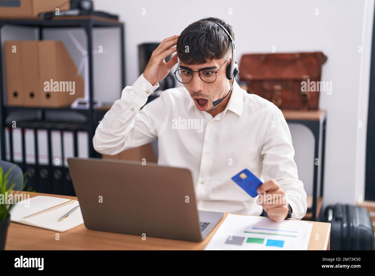 Young hispanic man working using computer laptop holding credit card ...