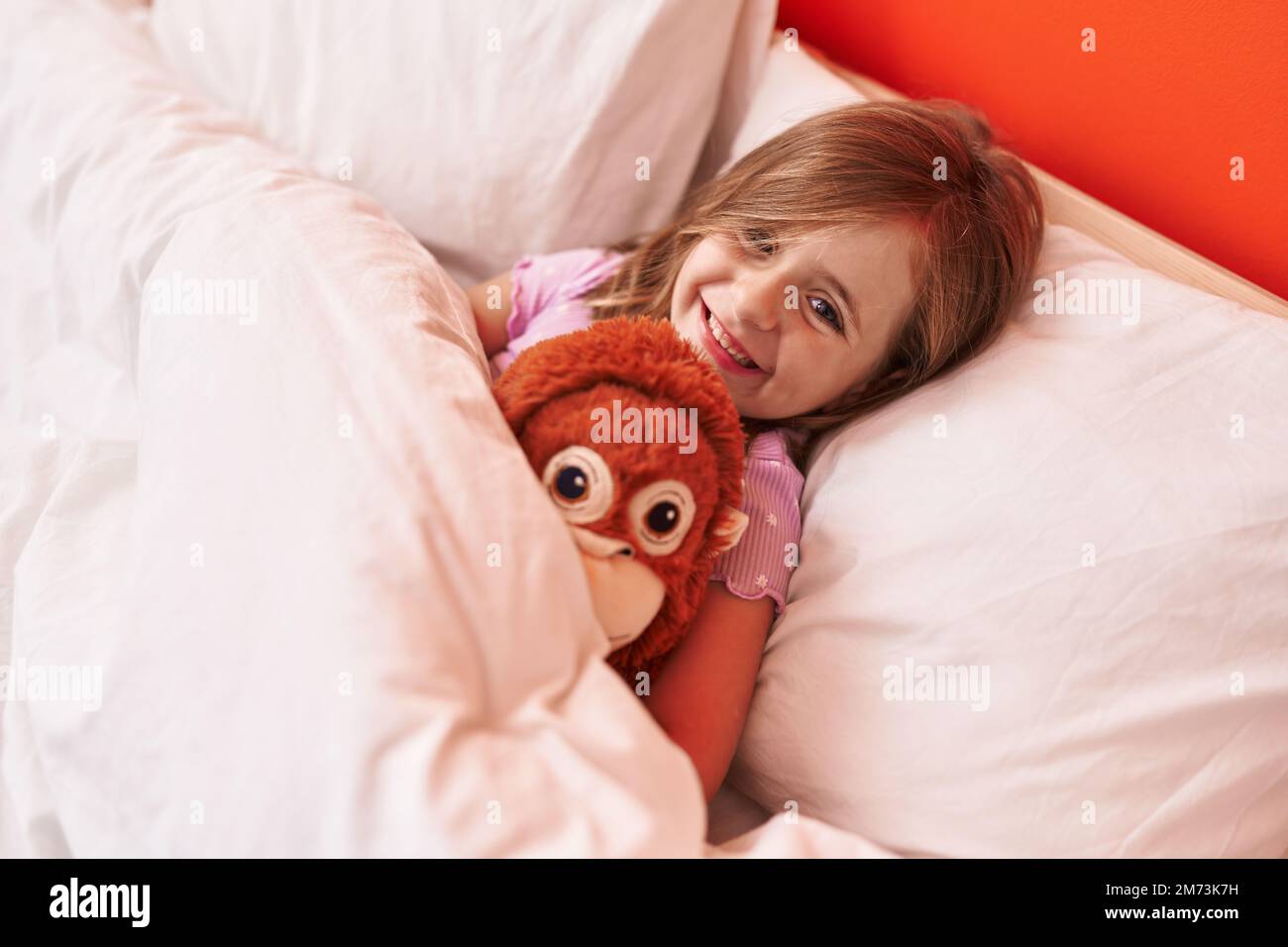 Adorable hispanic girl hugging monkey doll lying on bed at bedroom ...