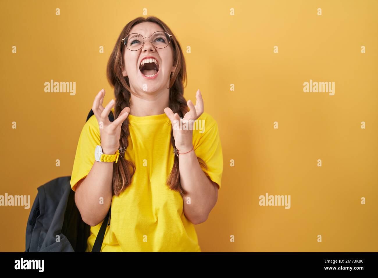 Young caucasian woman wearing student backpack over yellow background ...