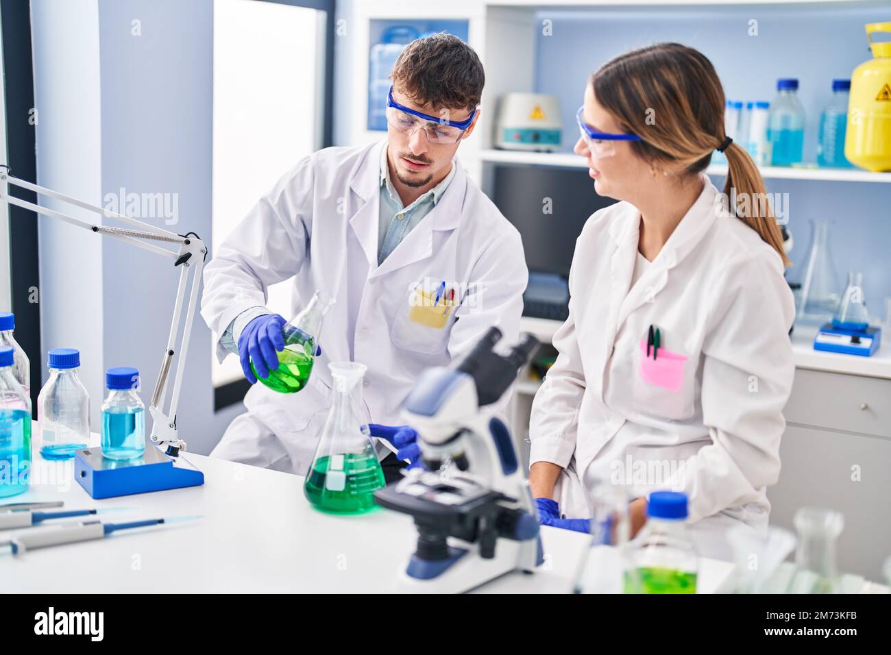 Young man and woman scientists workers measuring liquid at laboratory ...