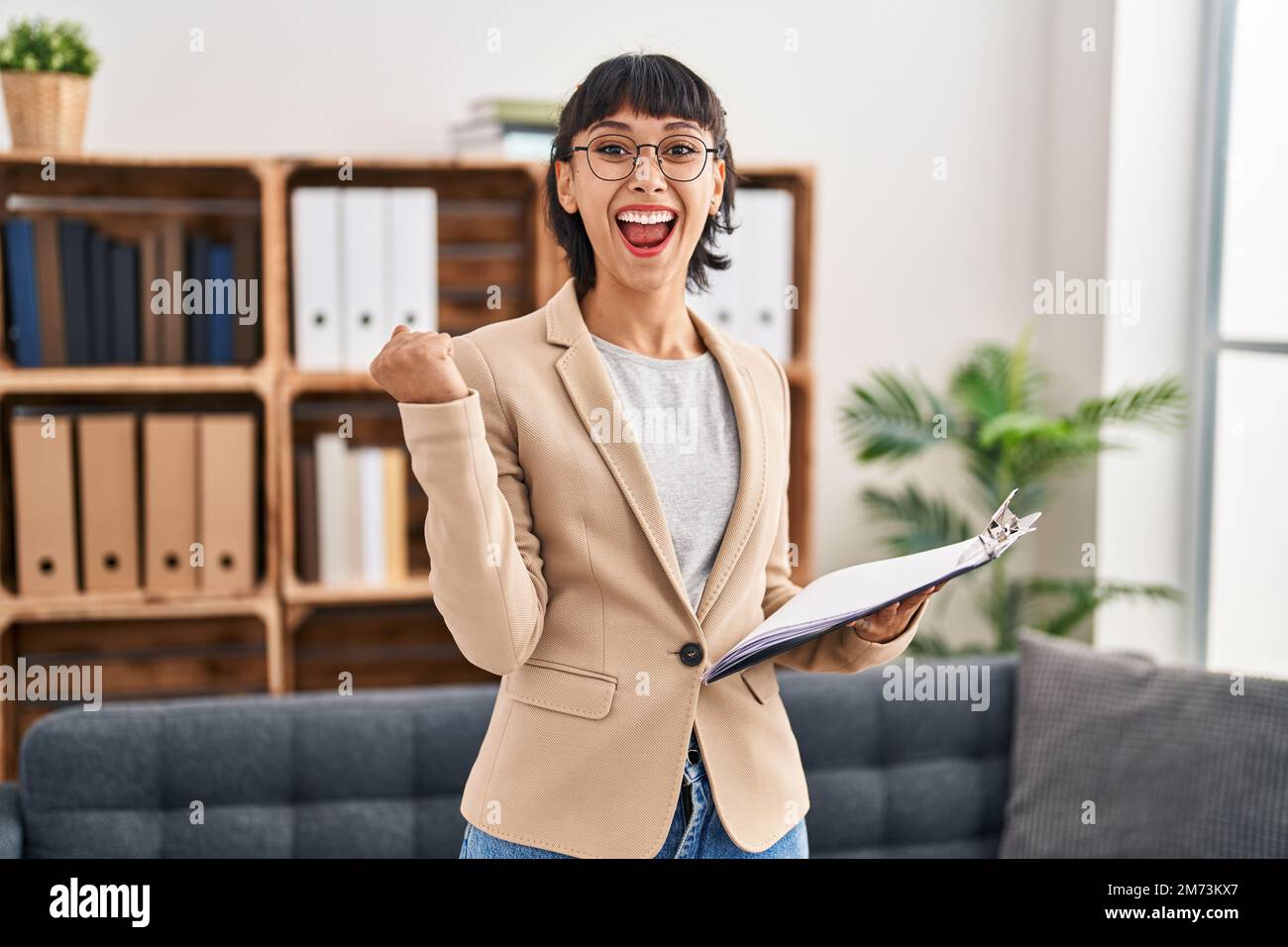 Young hispanic woman working at consultation office screaming proud ...