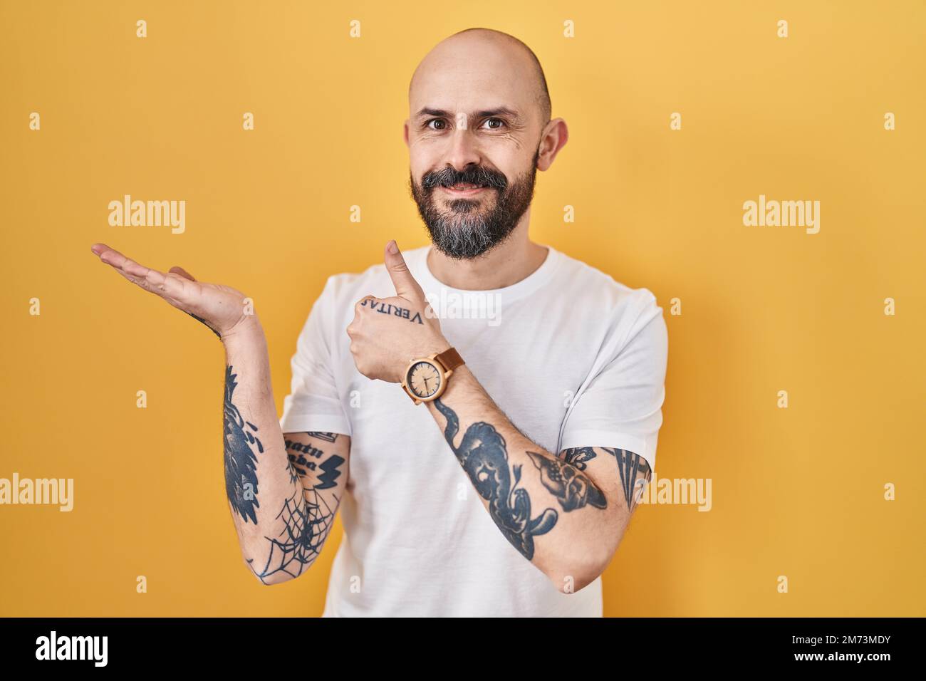 Young hispanic man with tattoos standing over yellow background showing ...