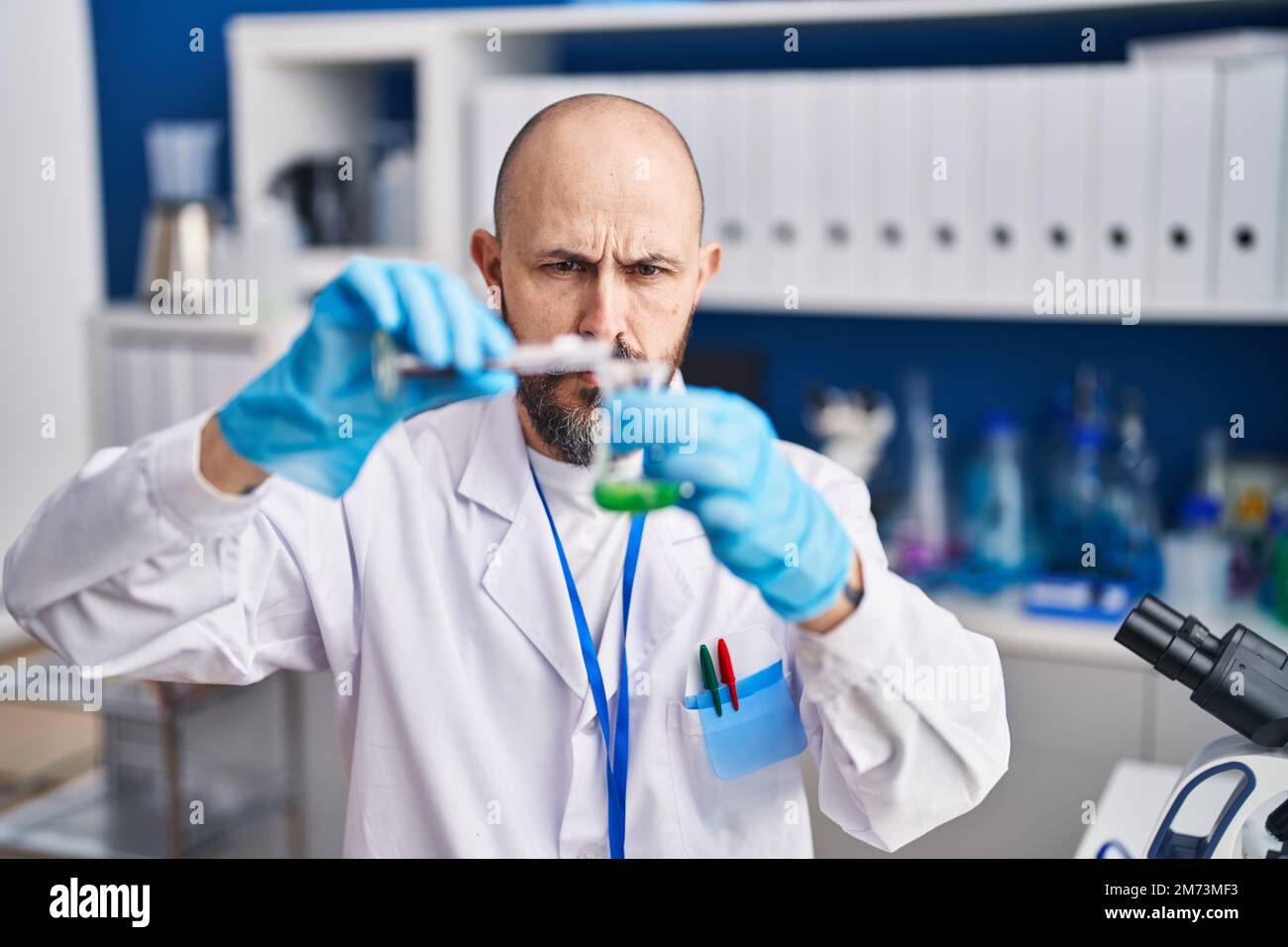 Young bald man scientist pouring liquid on test tube at laboratory ...