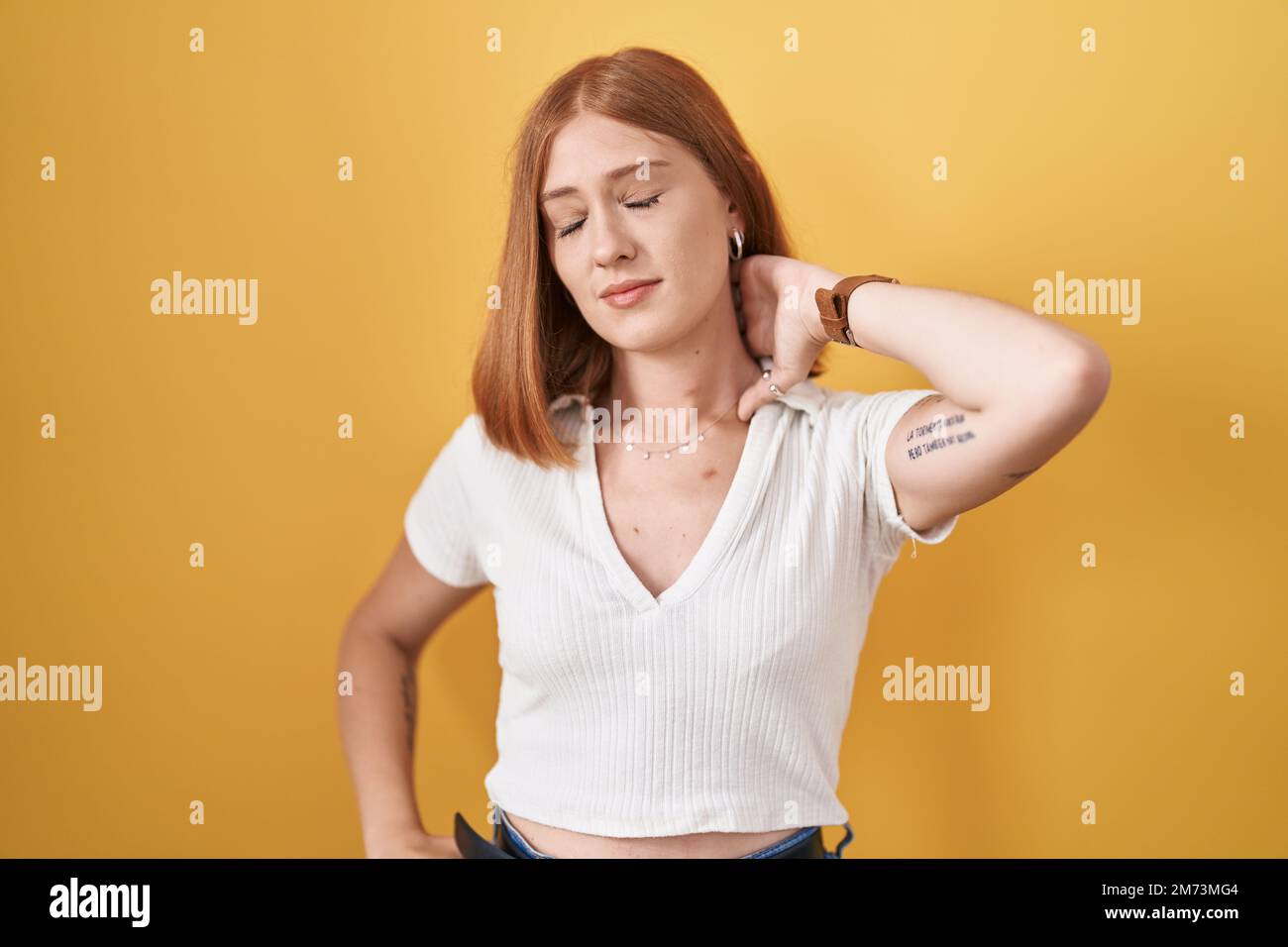 Young redhead woman standing over yellow background suffering of neck ...