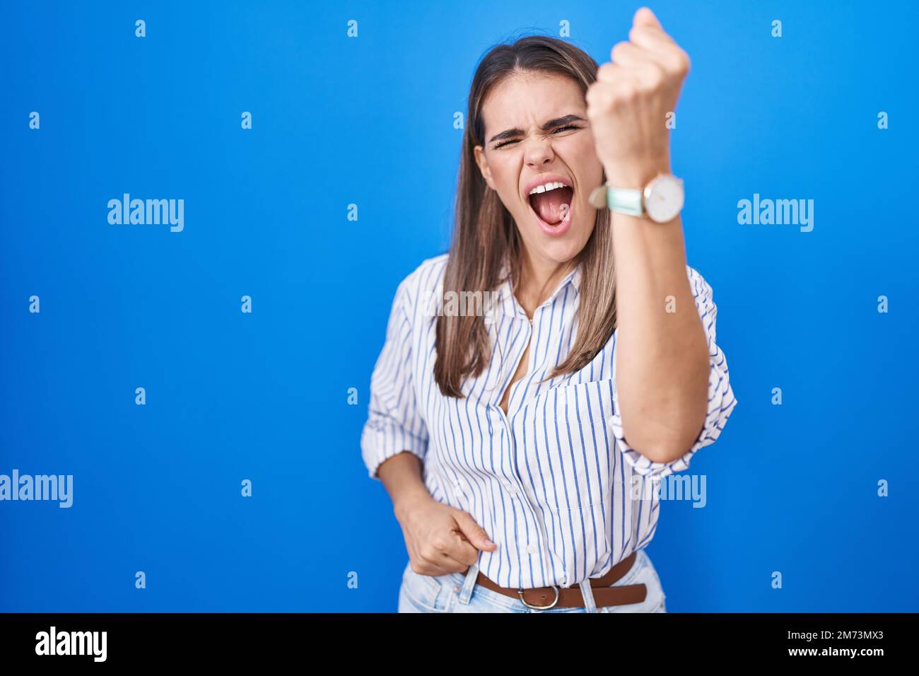 Hispanic young woman standing over blue background angry and mad ...