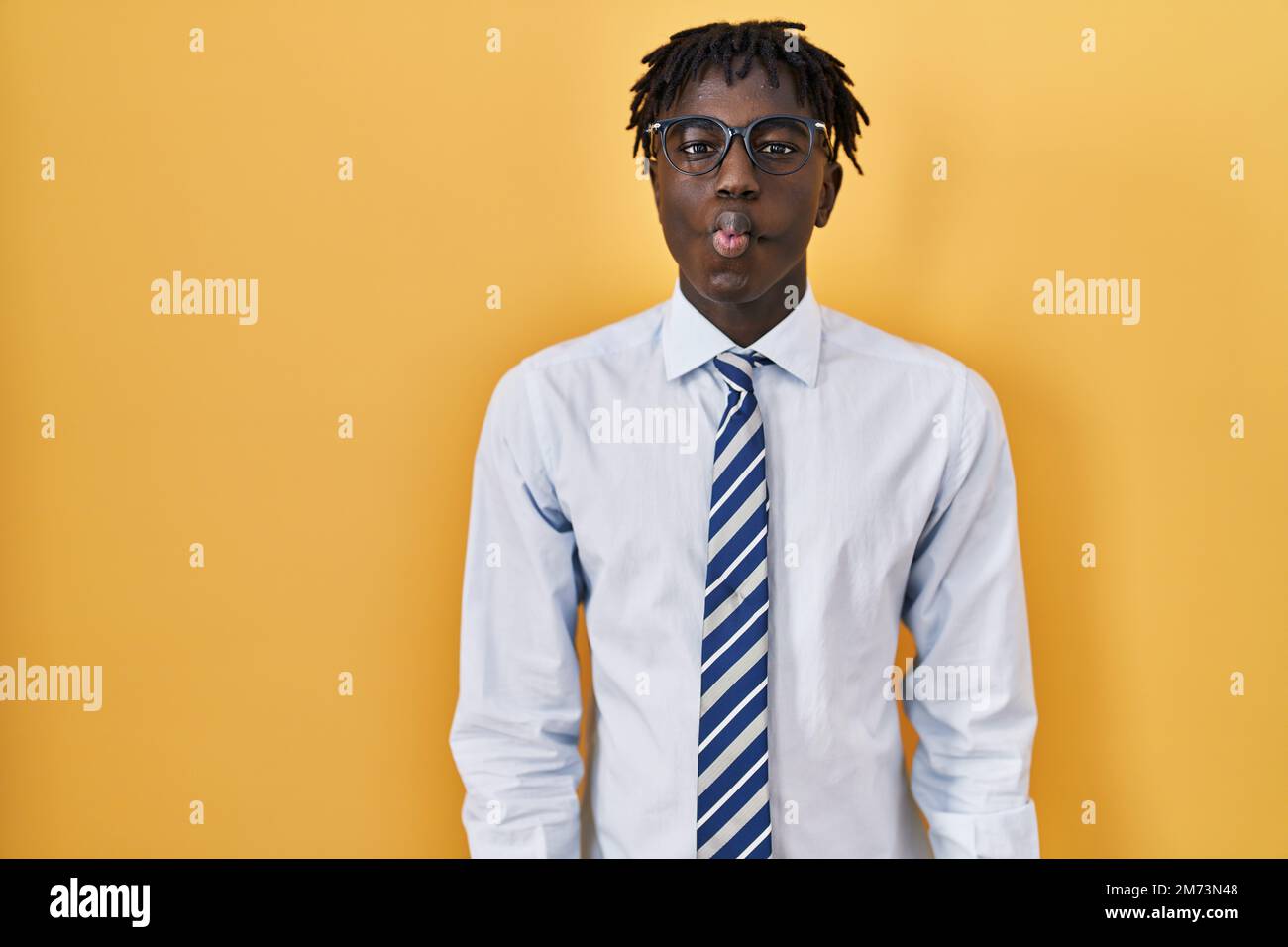 African man with dreadlocks standing over yellow background making fish ...
