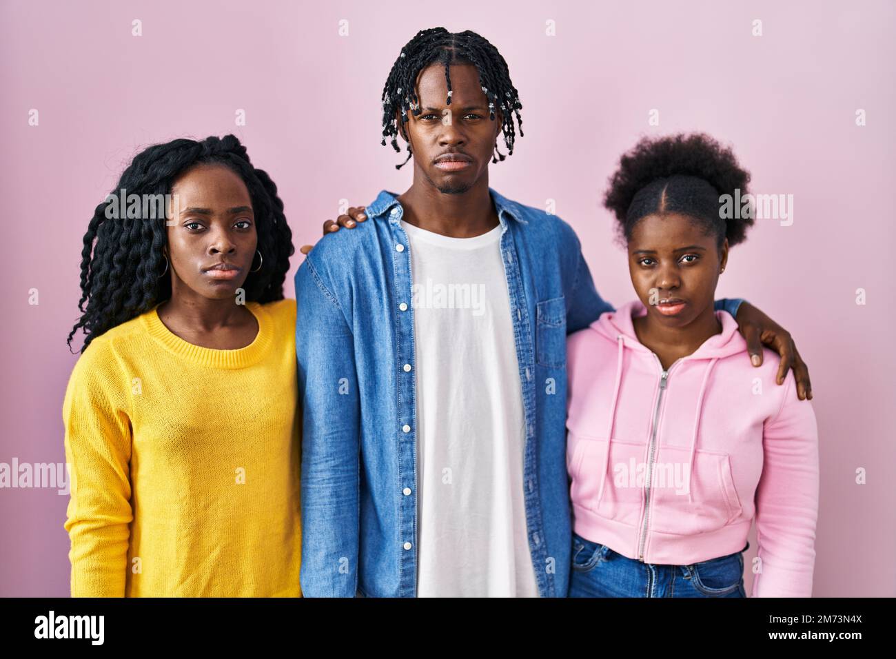 Group of three young black people standing together over pink ...