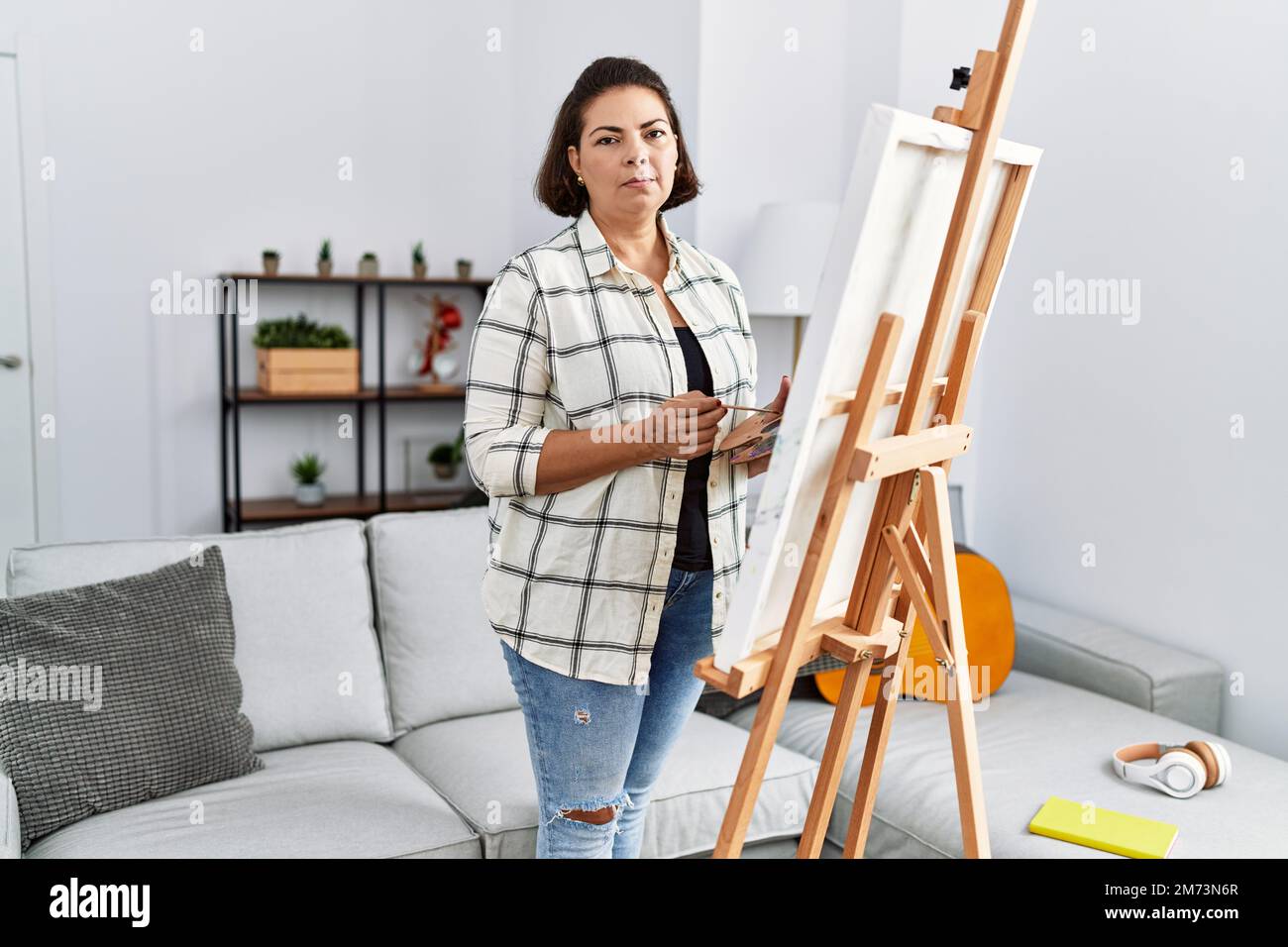Middle age hispanic woman drawing by painter easel stand at home ...