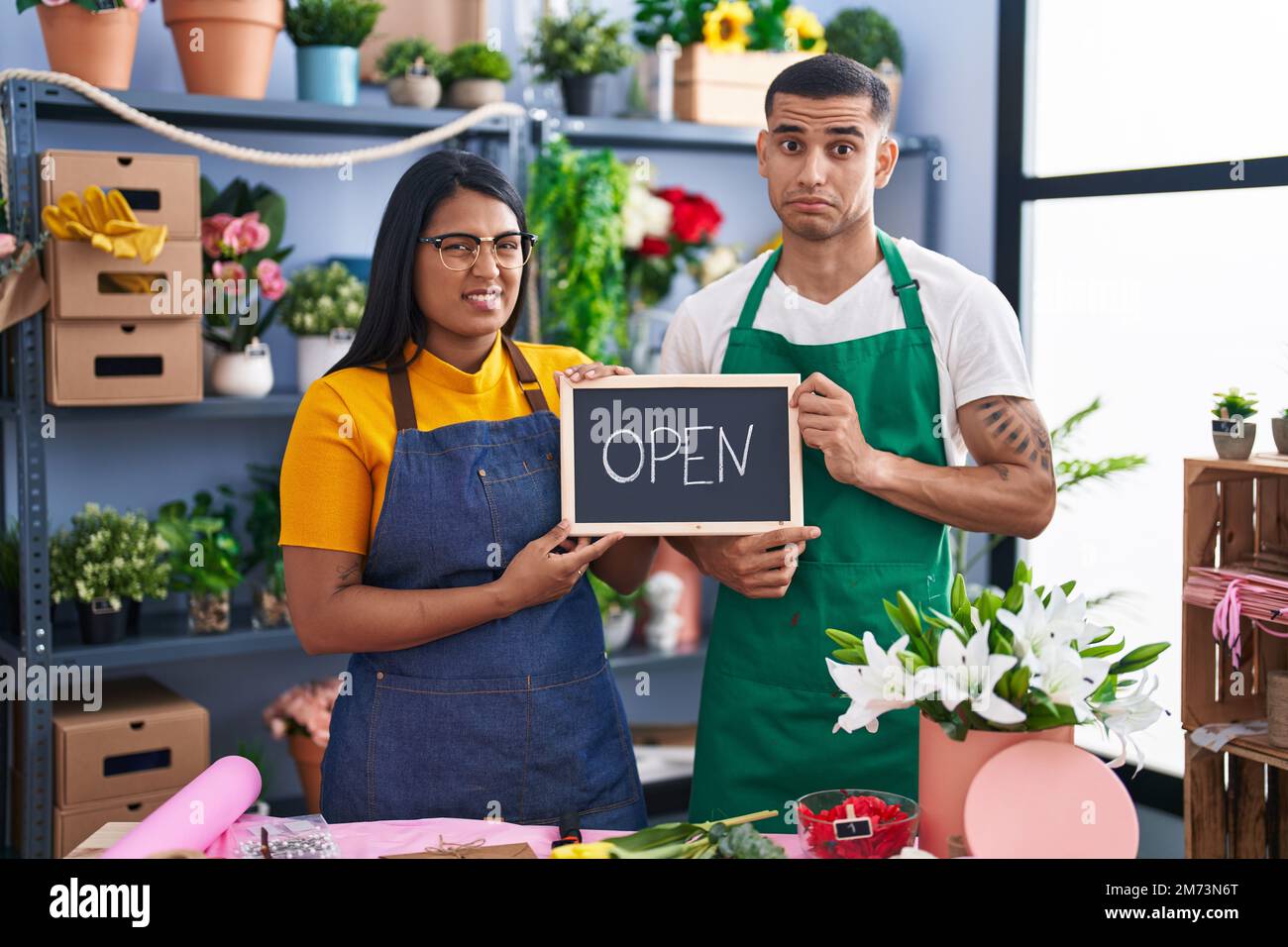 Young hispanic couple working at florist with open sign clueless and ...